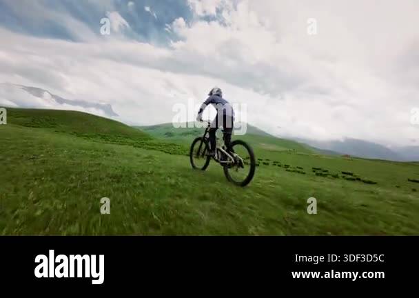 Side shot of cyclist riding mountain bike on green grass covered ...