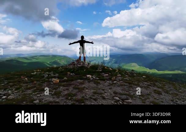 AERIAL SHOT - A fit young man runs to the top of a hill and raises his ...
