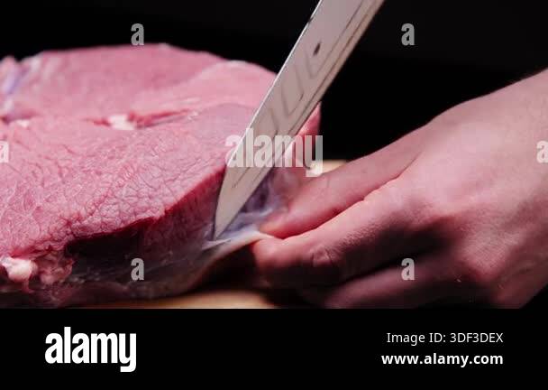 A butcher removes the fascia from a beef steak with a large knife in a ...