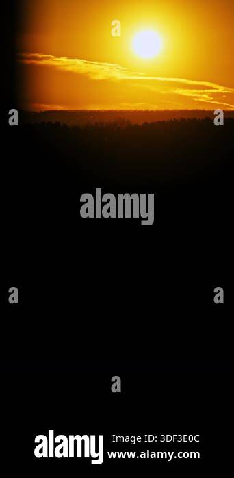 Bright sun sets in a vibrant orange sky above a dark forest silhouette ...