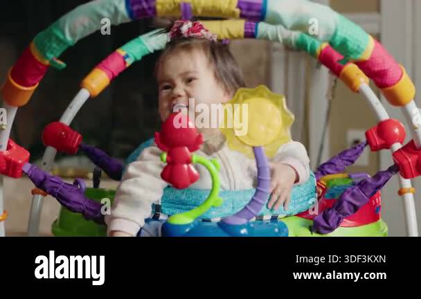 Baby girl bouncing playfully in a colorful activity jumper, making a ...