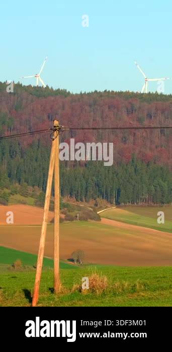 Wind turbines rotate in the background as electric poles line a path ...