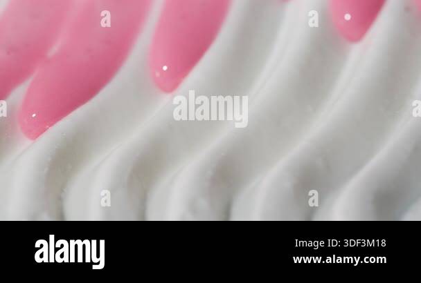 A person carefully applies pink icing on top of a white cake. The cake ...