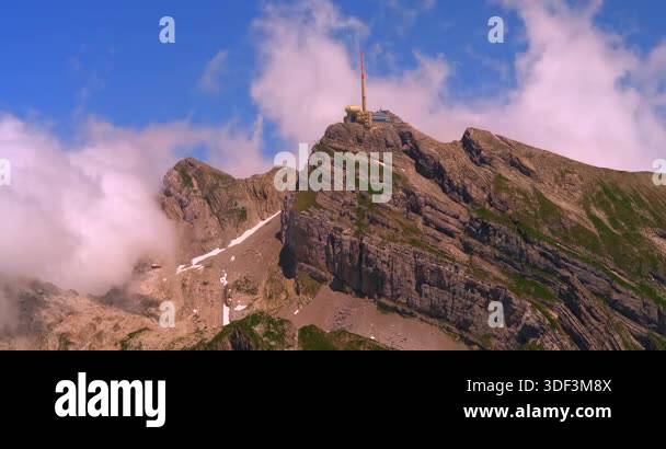 Hikers walk near a mountain peak with an observation tower at the top ...