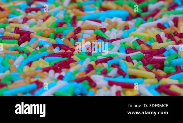Bright colors of sprinkles are spread evenly on a flat surface. Various ...