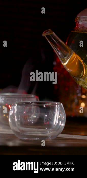 Hot tea is poured into glass cups, creating steam that rises in the ...