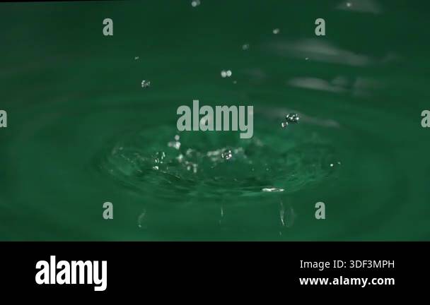 A water drop falls onto a green surface and creates a splash. The ...