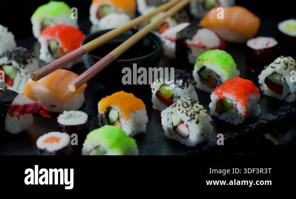 Various types of sushi are arranged on a black platter. Chops sticks ...