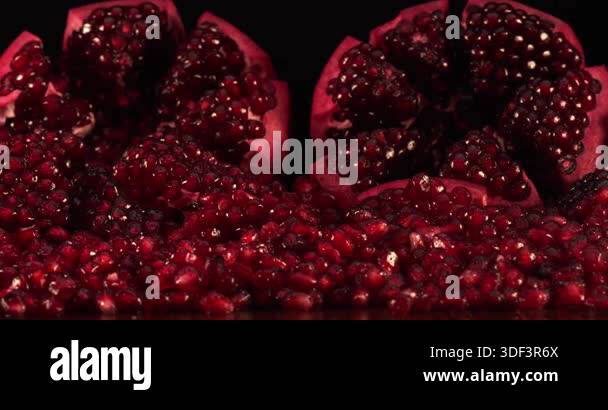 Pomegranate fruits are cut open to reveal bright red seeds placed on a ...