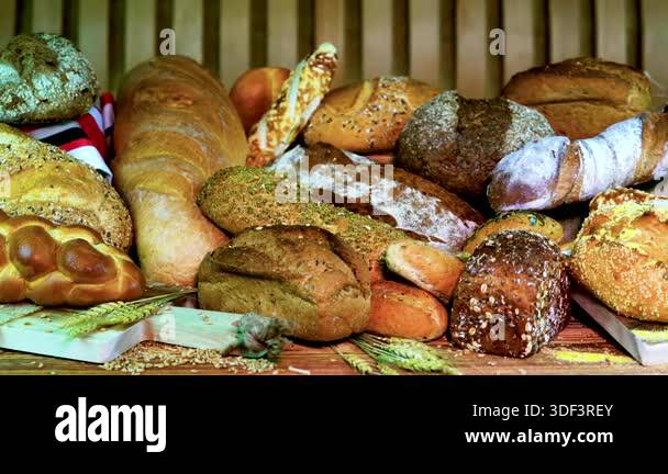 Different kinds of bread are on a wooden table. The breads include ...