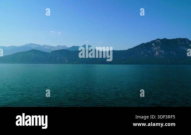 Clear blue sky shows mountains and calm lake water under sunlight. The ...