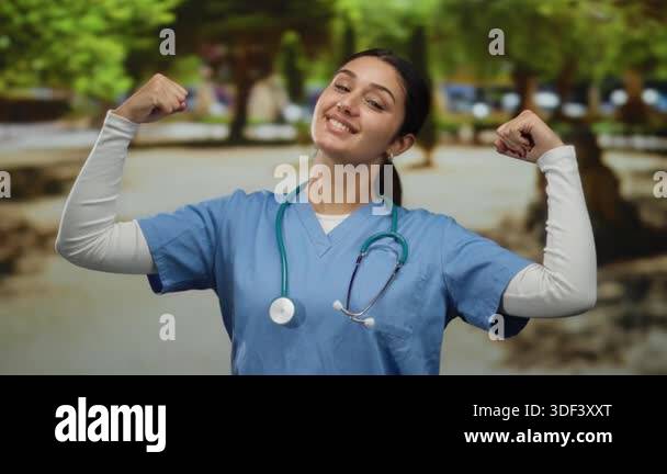 Hispanic woman in scrubs posing confidently with flexed arms in a sunny ...