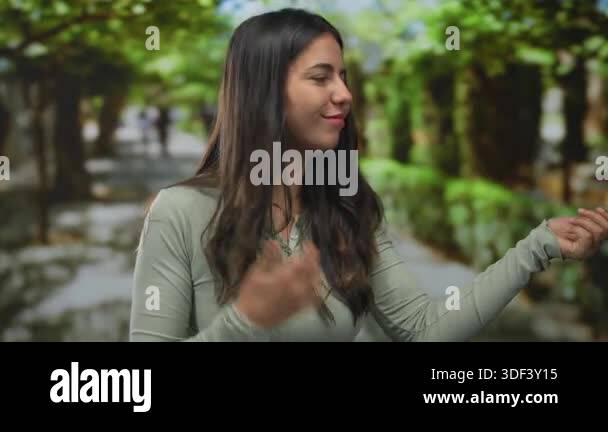 Young hispanic woman strums guitar gesture with hands along leafy green ...