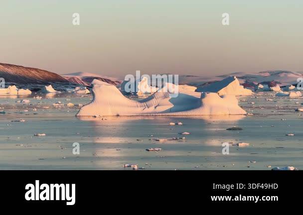 Icebergs drift slowly in clear water as the sun sets over a remote ...