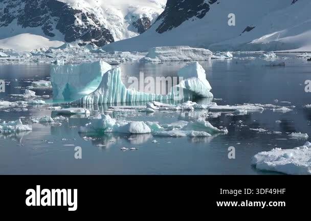 Icebergs drift slowly in clear water as the sun sets over a remote ...