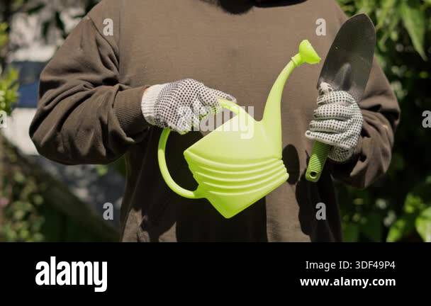 Person holding a small garden trowel in one hand and a watering can in ...