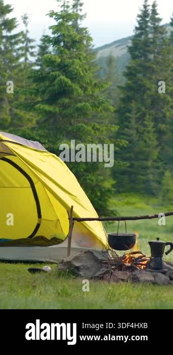 Yellow camping tent with campfire and cookware in mountain forest ...