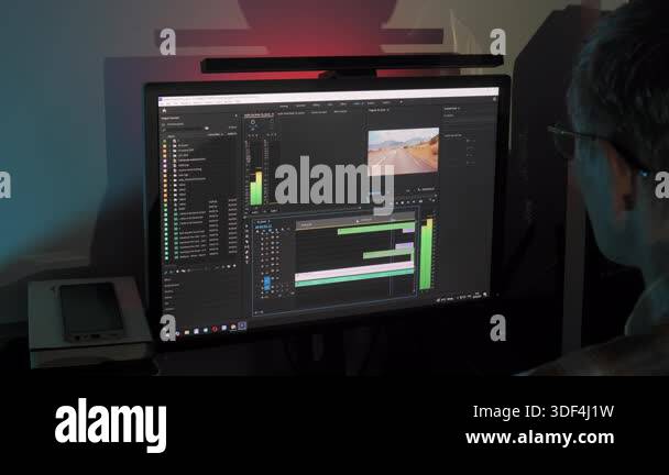 A man edits videos on a computer monitor in a dark workroom a ...