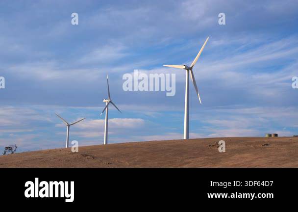 Wind turbine rotating gently against a blue sky with golden sunlight in ...