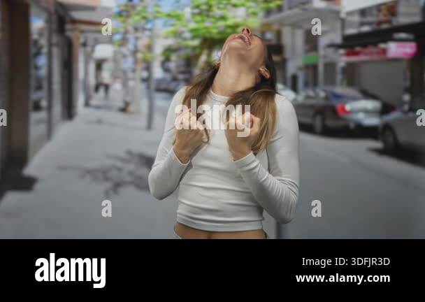 Woman with clenched fists and head thrown back on a busy street ...