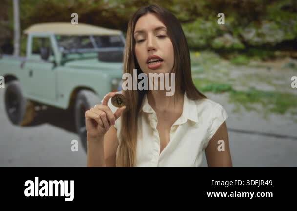 Woman holds bitcoin coin between thumb and forefinger in green park ...