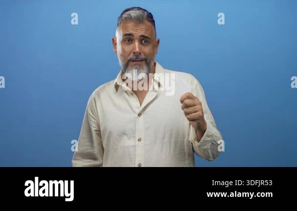 Bearded middle age man holding creditcard and raising palm in blue ...
