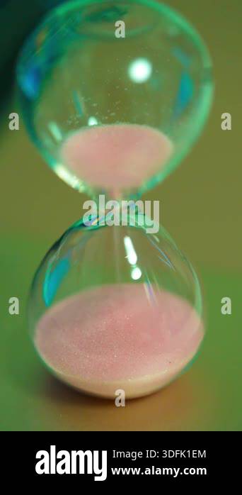 Sand flowing inside hourglass standing on surface. Pink grains running ...