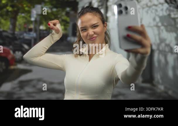Young hispanic woman flexes arm muscle while taking a selfie with her ...