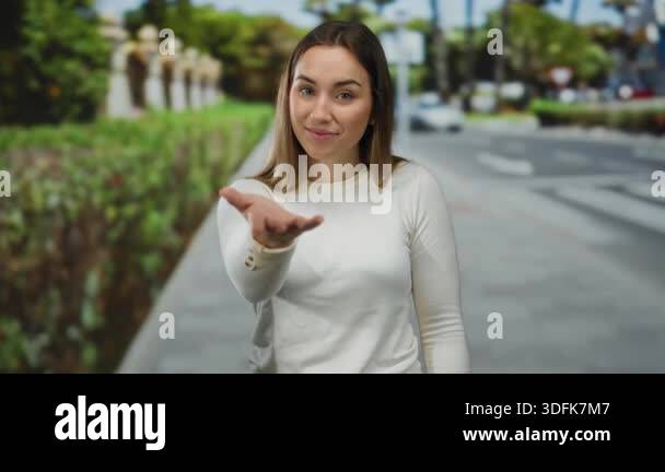 Woman extending hand to camera with a smile in an outdoor street ...