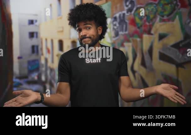 Man in staff uniform with afro shrugging on graffiti street background ...