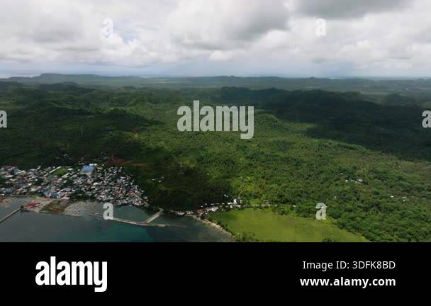 Coastal village with lush green hills and cloudy sky creating a ...
