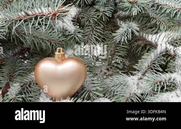 A golden heart-shaped New Year's decoration swings on a snow-covered ...