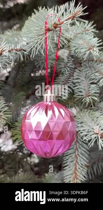 A pink faceted Christmas decoration swings from a fir branch in a ...