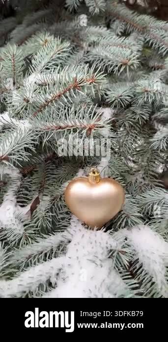 A golden heart-shaped New Year's decoration swings on a snow-covered ...