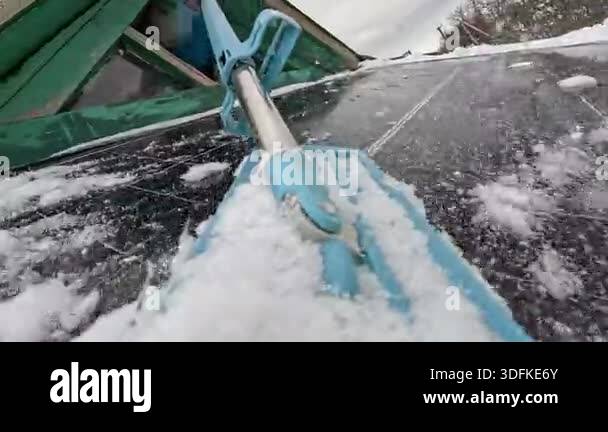 A girl cleans the solar panel from snow on the roof of a house using a ...