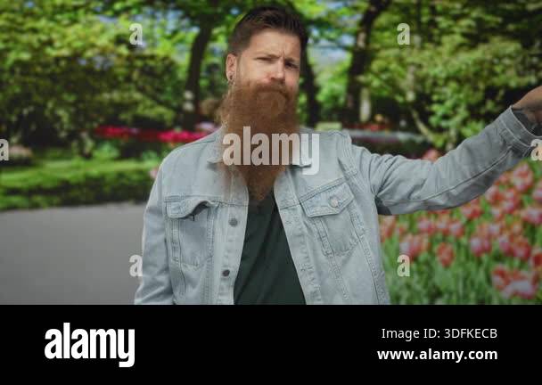 Young man with long beard pointing finger at oak tree in green forest ...