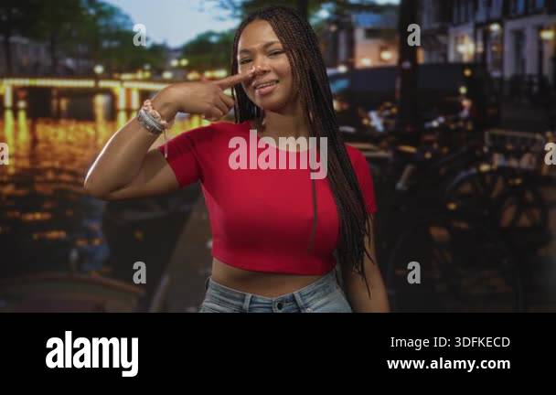 Woman finger to nose gesture smiling in red crop top and jeans on canal ...