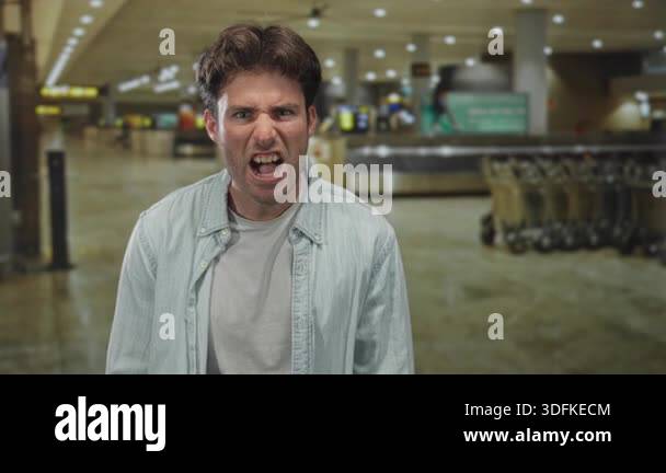 Man shouting mouth open facing camera at airport terminal near baggage ...
