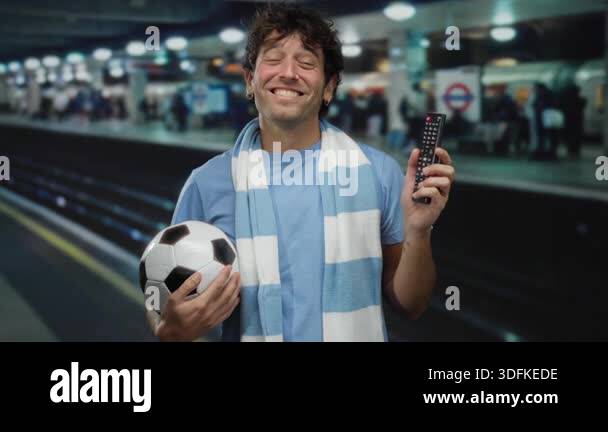 Hispanic man in subway holding football and remote smiling in ...