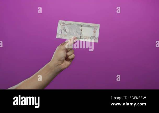 Man holding a united arab emirates dirham against a vibrant pink wall ...