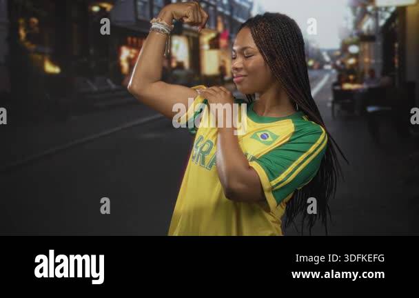 Woman flexes bicep and points to muscle on a city street wearing yellow ...