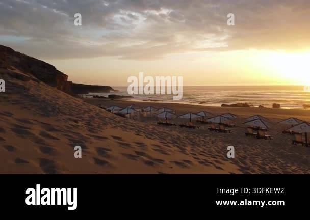 sunset sand dune overlooking empty beach with cabanas and footprints ...