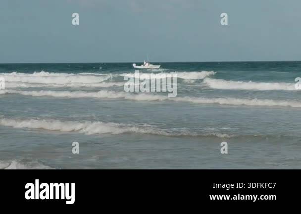 A small fishing boat moves across rough ocean waves near coastline on a ...