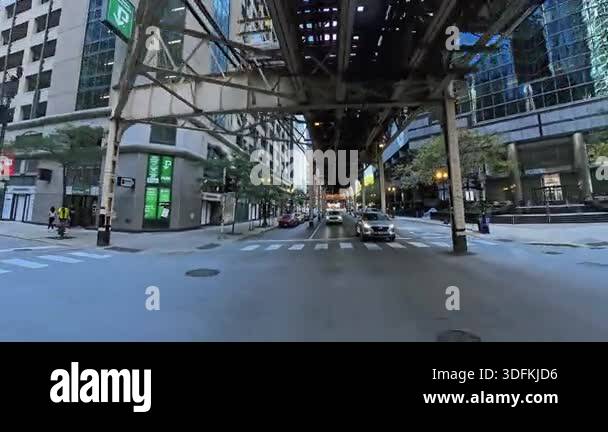 POV of a modern city street beneath elevated railway tracks, traffic ...