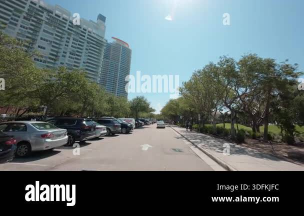 Urban street from a moving car, showing parked vehicles, high-rise ...