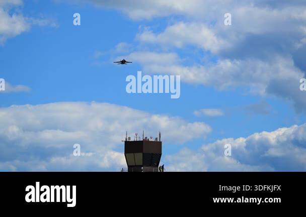 Military fighter jet fly past an airport control tower against a blue ...