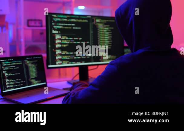 A mysterious hooded hacker working on a computer in a dark room. A ...