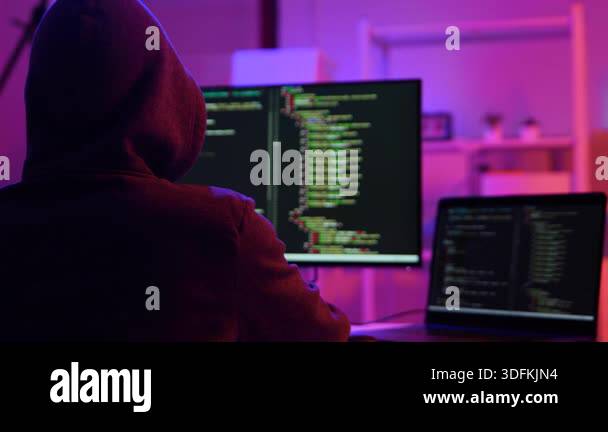 A mysterious hooded hacker working on a computer in a dark room. A ...