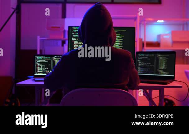 A mysterious hooded hacker working on a computer in a dark room. A ...