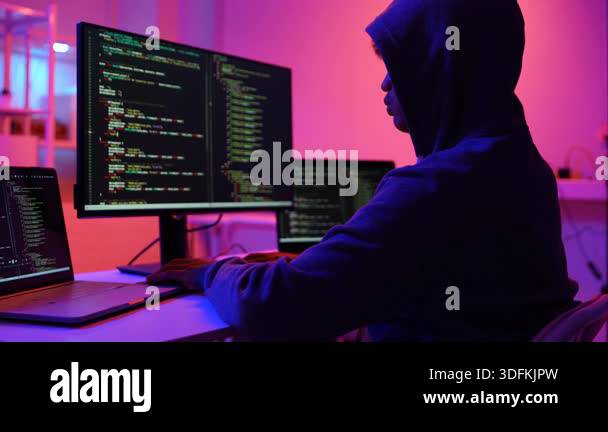 A mysterious hooded hacker working on a computer in a dark room. A ...